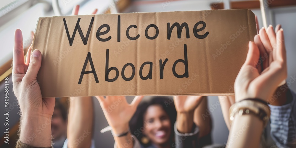 A 'Welcome Aboard' sign is held up by hands in a crowd, symbolizing ...
