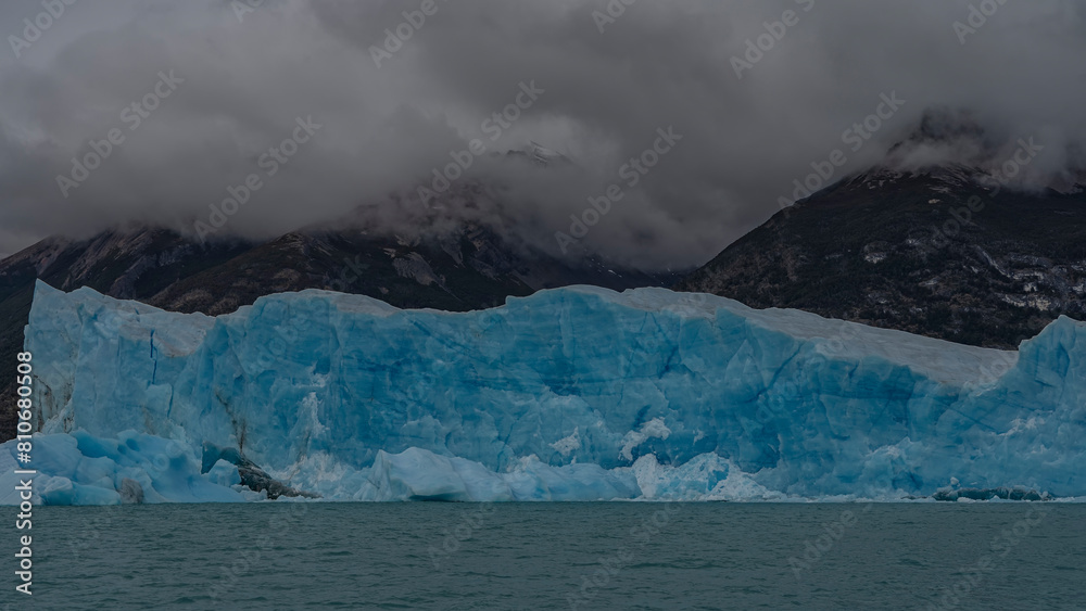 A block of blue ice rises like a wall above a glacial lake. Coastal ...