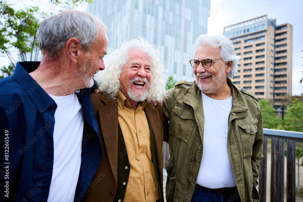Group of three mature caucasian men enjoying embracing walk together laughing outdoor. Senior ...