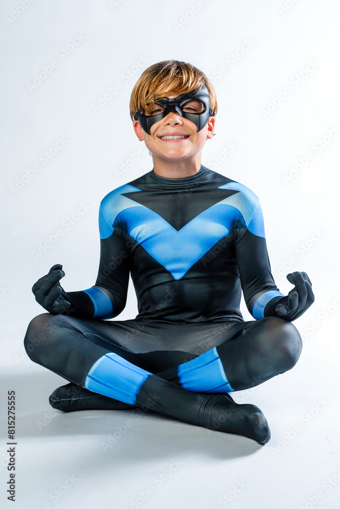 Young male masked superhero sitting legs crossed in a relaxed yoga pose ...