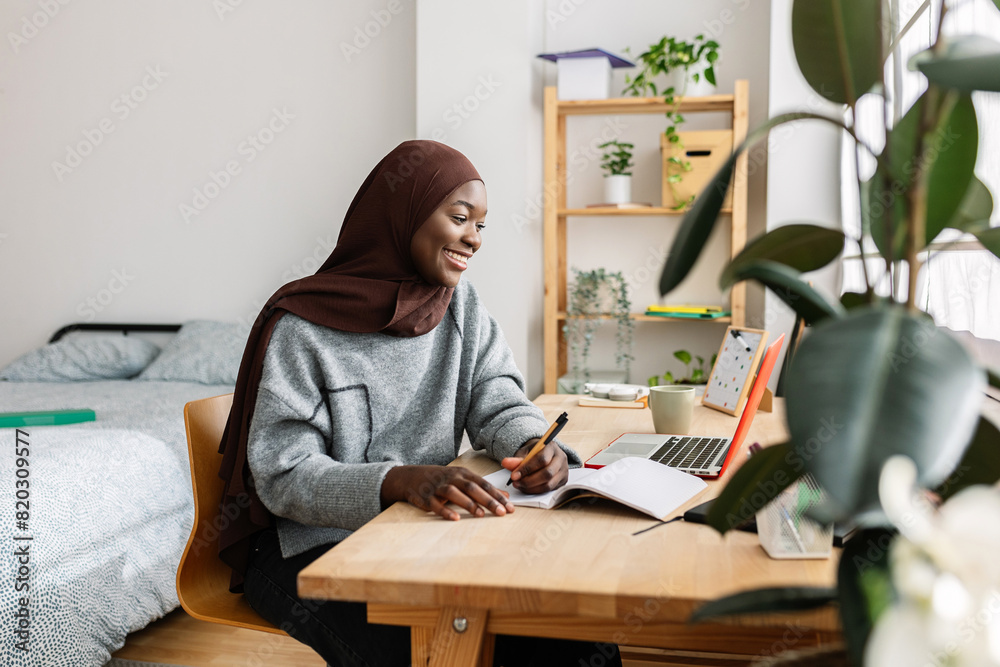 Young adult african student woman taking notes while using laptop ...
