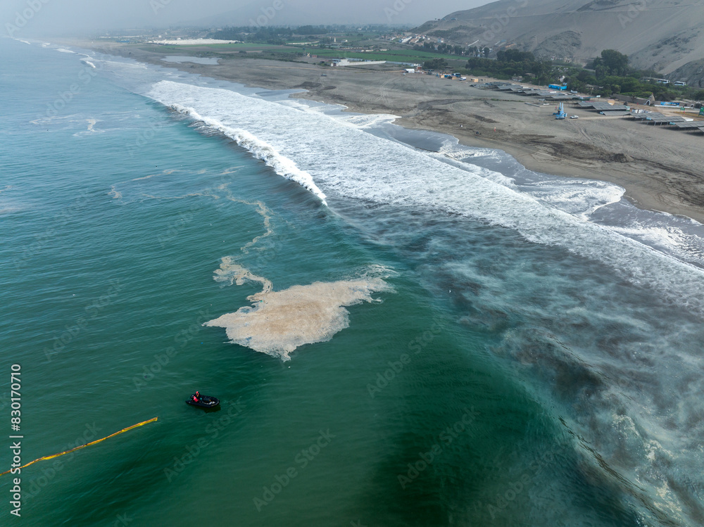 Boat deploying containment barriers against an oil spill at Chancay ...