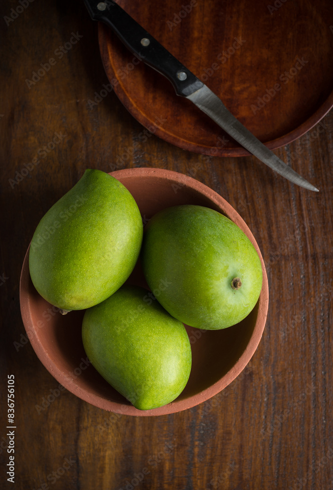 Fresh, big raw mangoes placed in a an earthen bowl, view from top ...