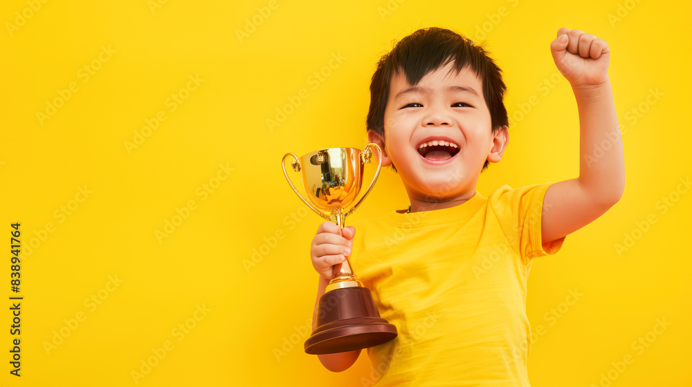 Little Asian boy celebrates victory holding his golden trophy on yellow ...