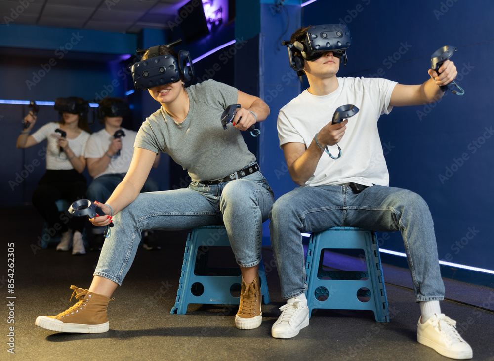 Male and female friend in helmets and with joysticks are sitting ...