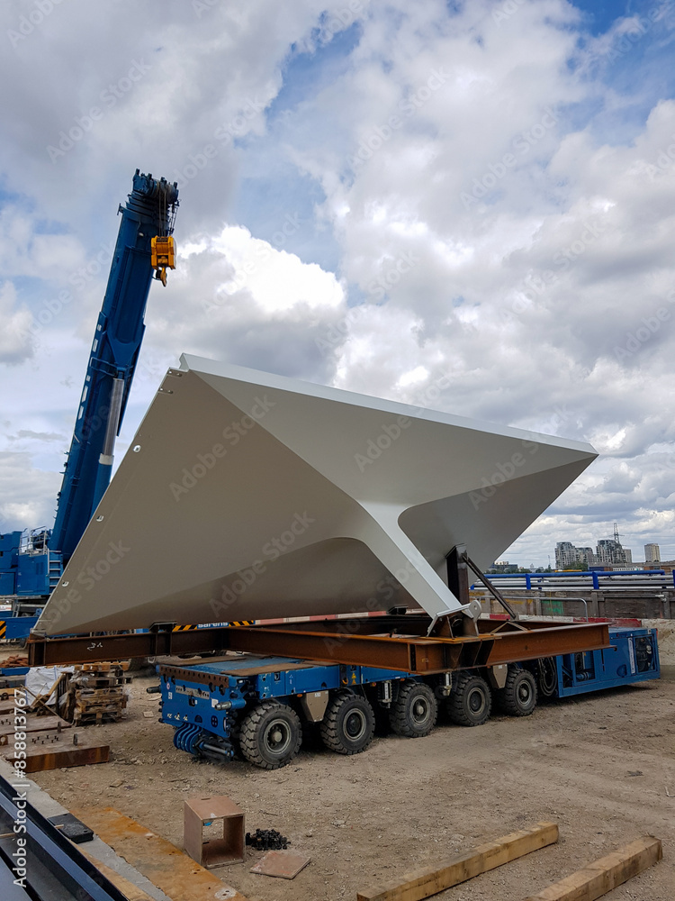 Crane lifting large bridge section onto self-propelled modular trailer ...