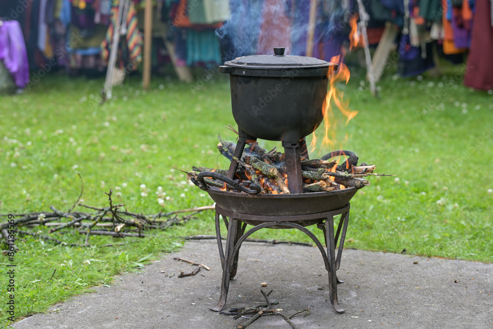 Fire brazier with burning wood and a three-legged iron cooking pot to ...