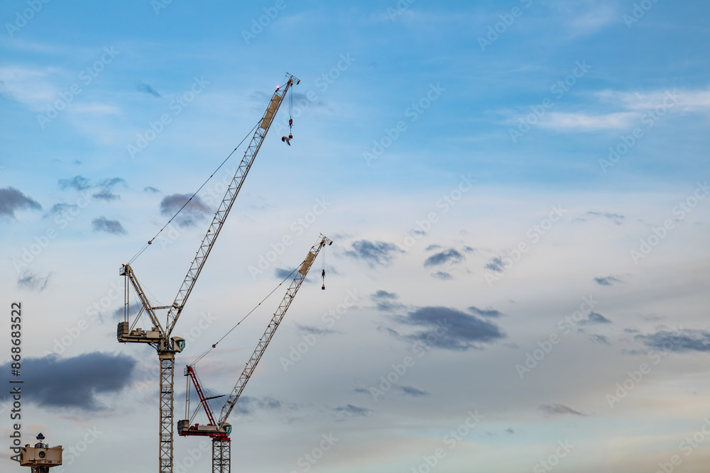 Two towering construction cranes stand parallel against a clear early ...