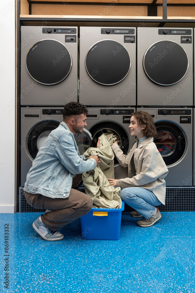 Young couple removing sheet from washing machine squatting in ...