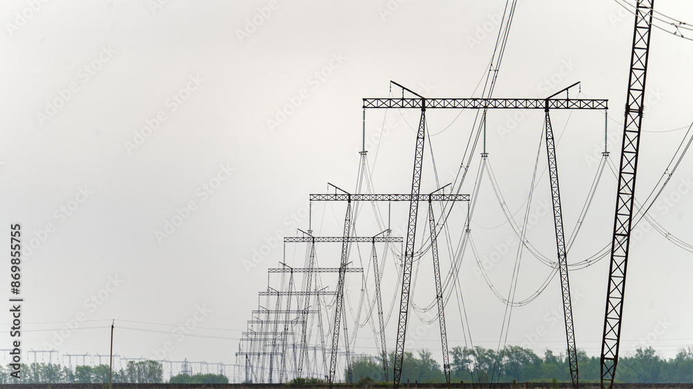 A long line of power lines stretching across a field. The sky is ...