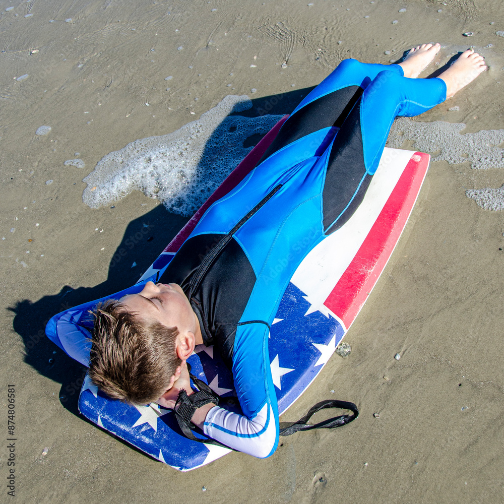 Relaxed young preteen beach boy swimmer lying on his boogie board in ...
