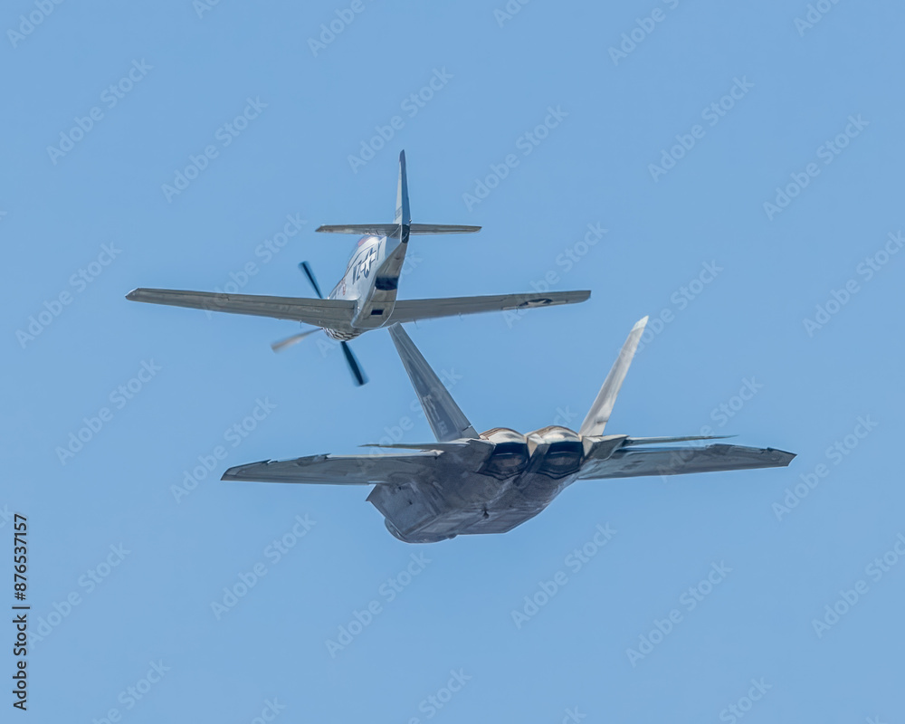 Rear view of P-51 Mustang and F-22 fighter fly in close formation at an ...