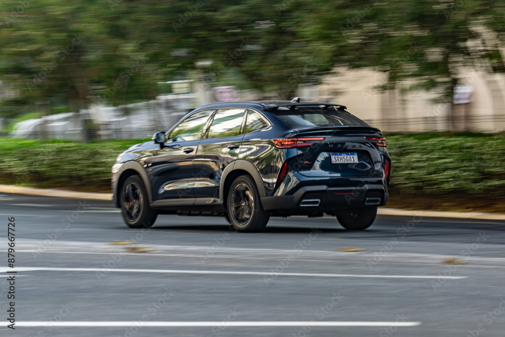 Dark blue GWM Haval H6 GT cruising city street, Hybrid SUV in movement ...