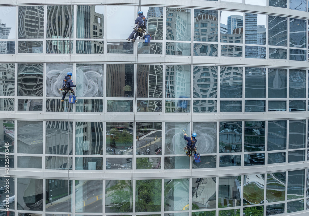 Professional alpinist window washers hang from a building in a harness ...