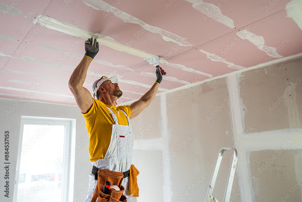 The worker make a plasterboard ceiling. He does taping plaster drywall ...