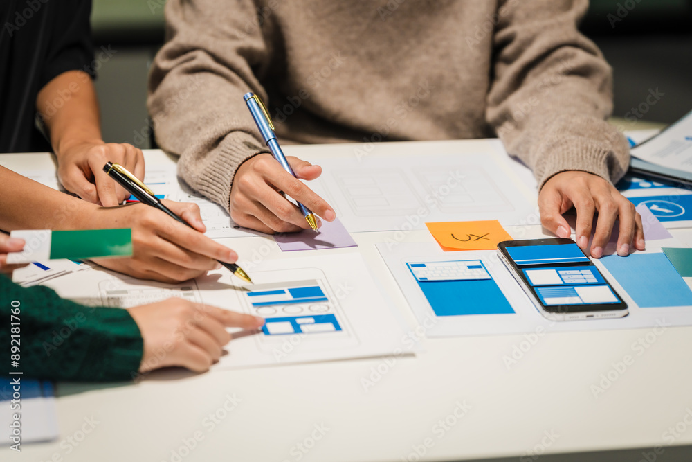 Close-up of hands working on UX/UI design at a desk. Papers with ...