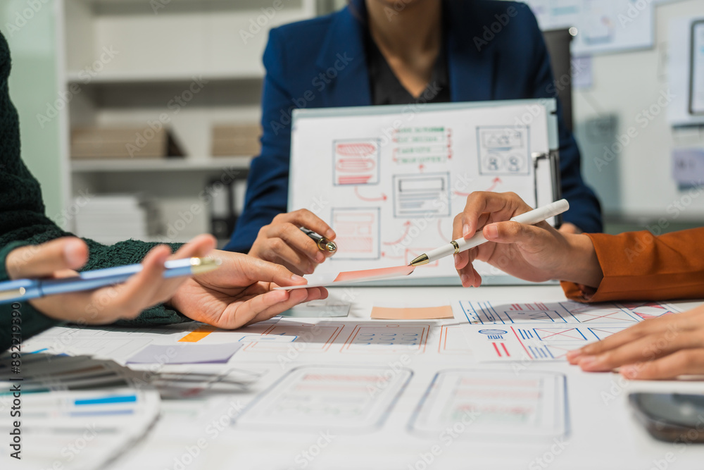 A group of people collaborates around a desk, discussing and reviewing ...