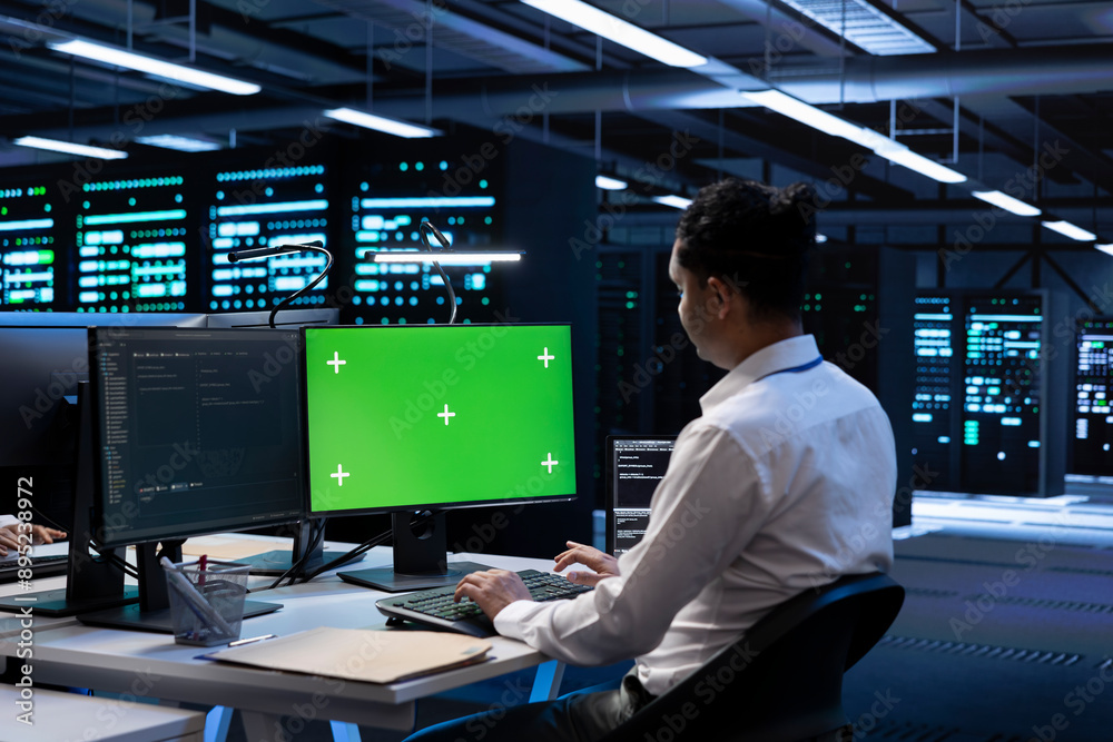 Admin in data center using diagnostic tools and system monitoring software on green screen PC to ...
