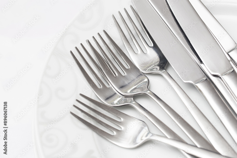 Silver cutlery on a white plate. Close-up of forks and knives set on ...