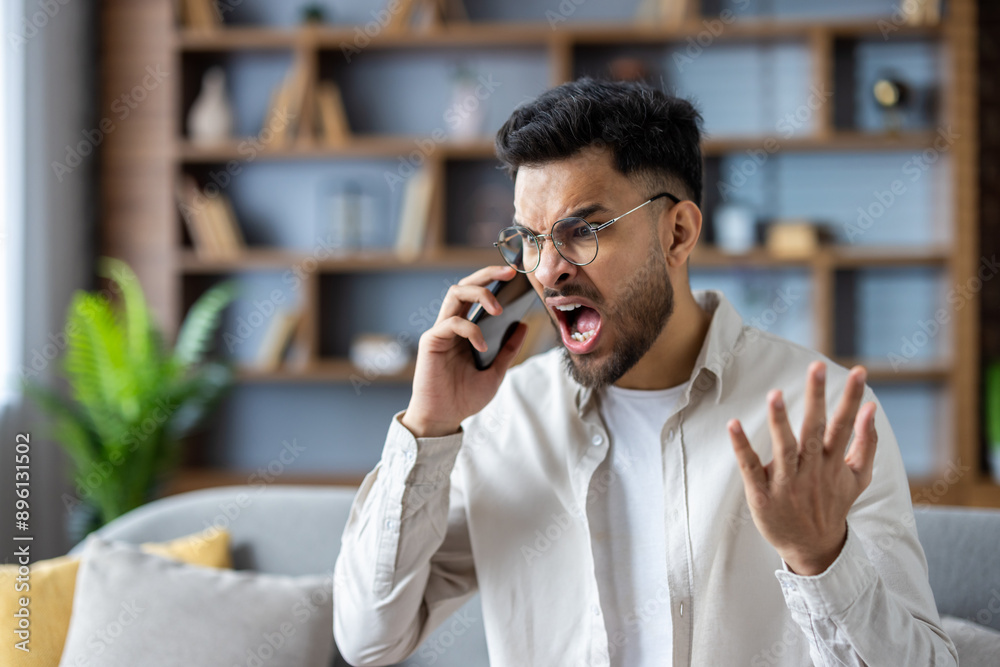 Angry man shouting on phone in modern living room expressing ...