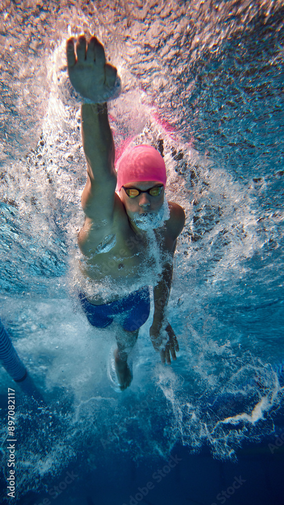 Athletic male swimmer captured mid-freestyle stroke underwater, displaying strength and ...