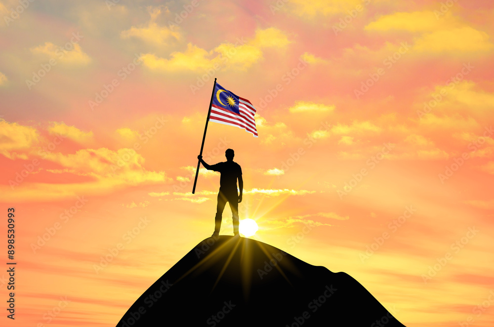 Waving flag of Malaysia at the top of a mountain summit against sunset ...