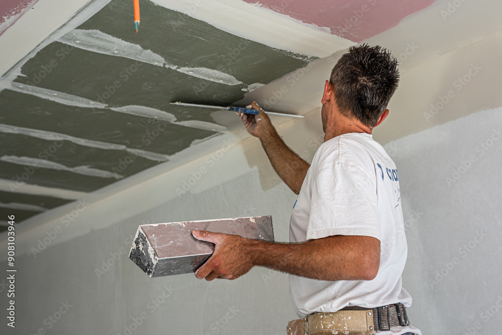 The worker make a plasterboard ceiling. He does taping plaster drywall ...