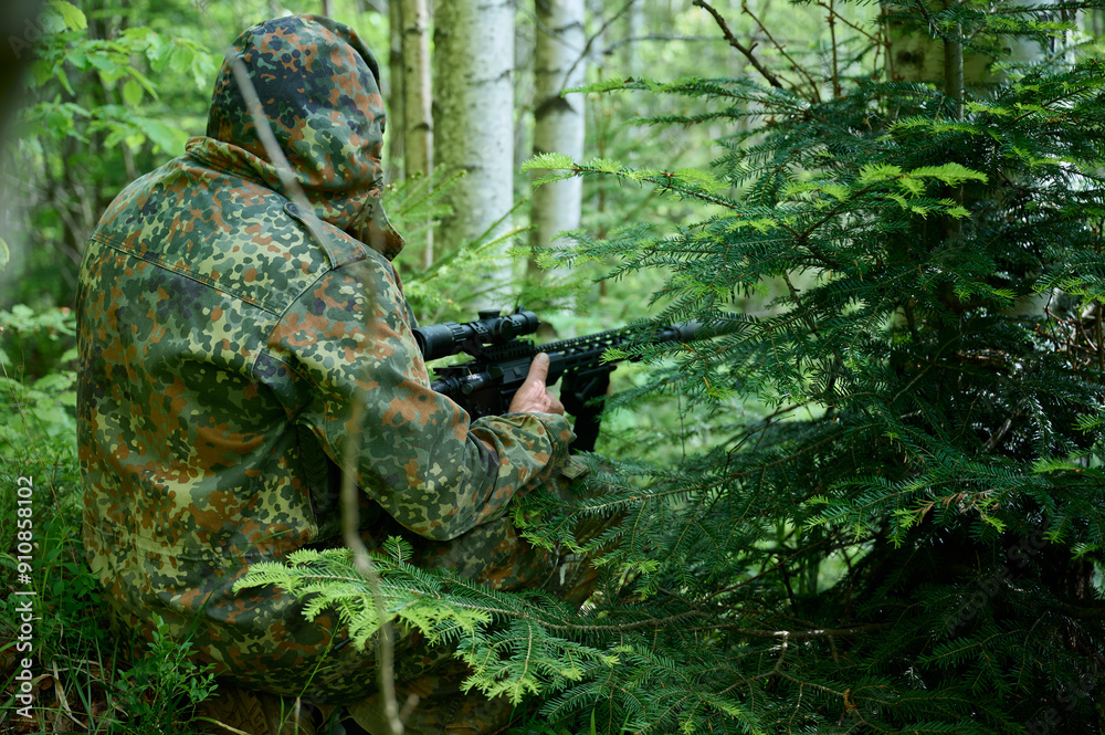 Hunter with rifle wearing camouflage suit sitting in ambush ...