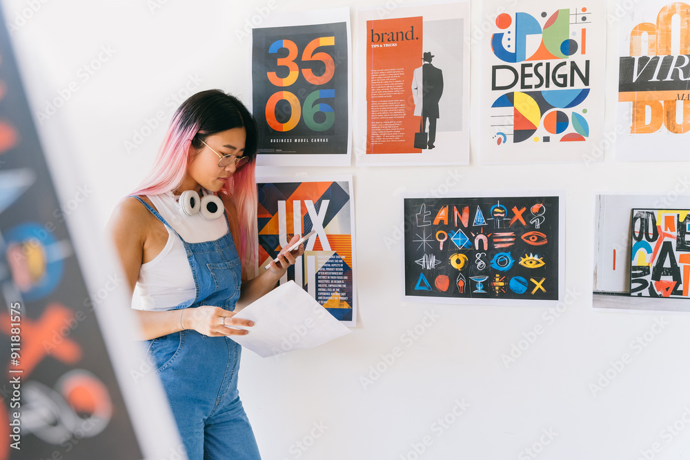 Chinese graphic designer reviewing work while standing besides posters ...