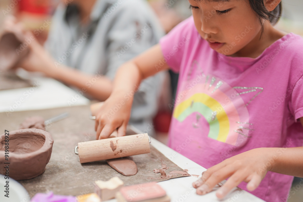 Young girl uses a rolling pin to flatten clay during an art class, Her ...