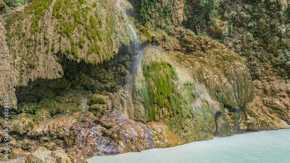 An exotic tropical waterfall. Thin streams of water flow down the mossy ...