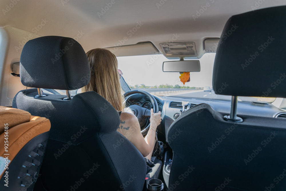 inside of a vehicle, seen from the backseat. A woman with light hair is ...