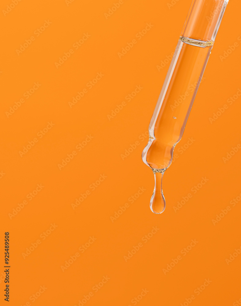 Glass cosmetic pipette with orange skin care serum and a hanging drop ...