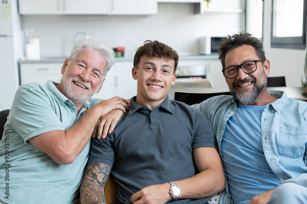 Happy multigenerational family of males stay together sitting on sofa smiling looking at camera ...