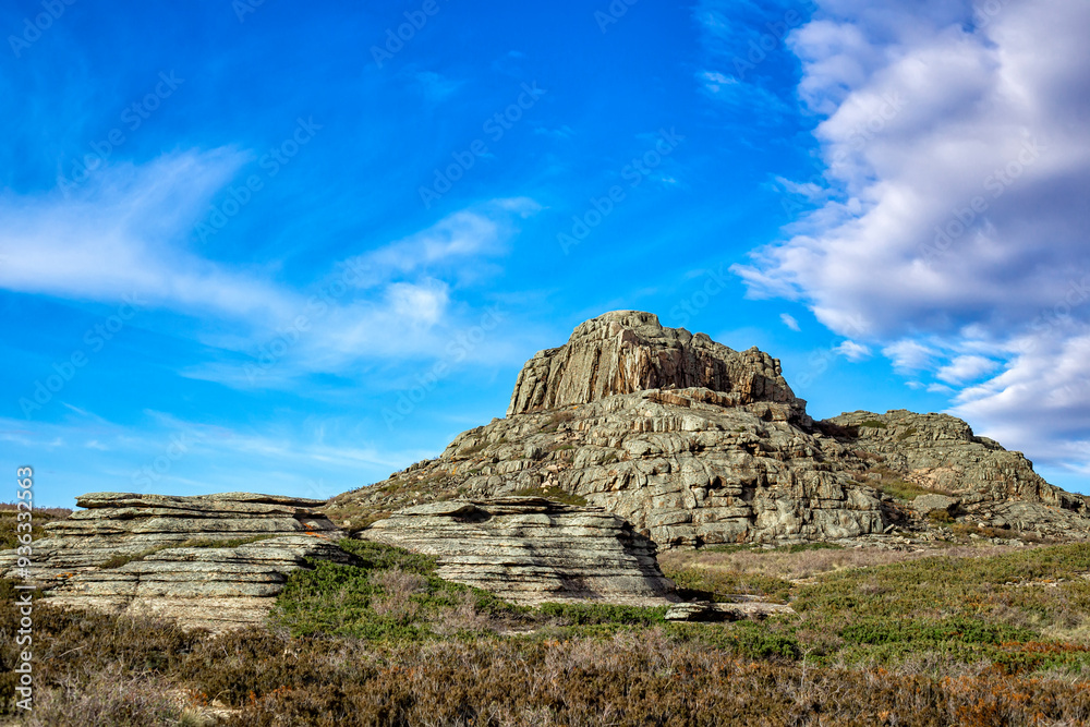 Lonely high stone crumbling mountain among rocks under blue sky with ...