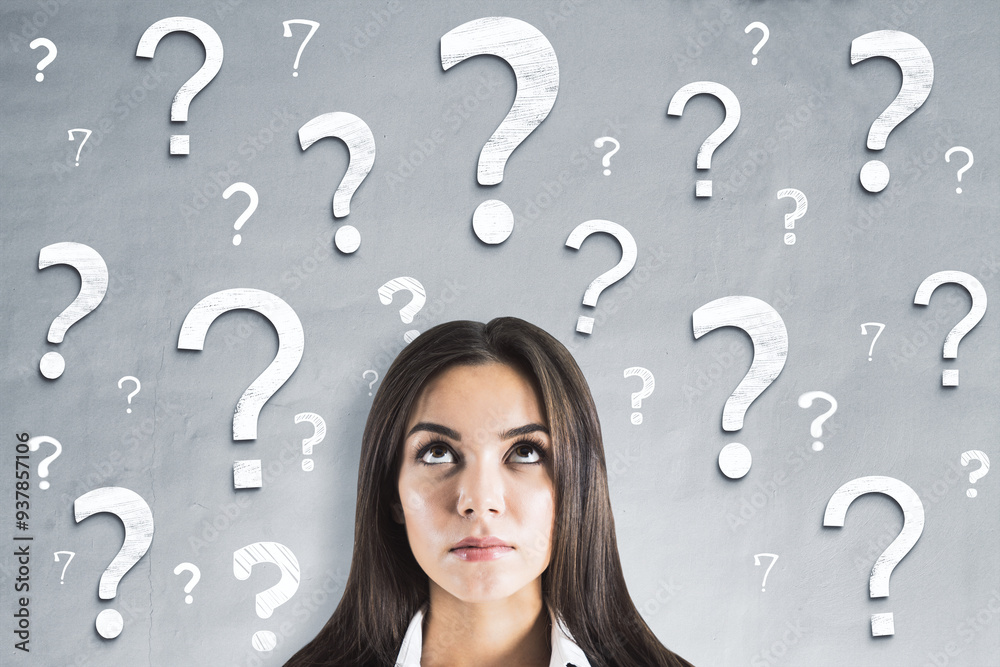 Woman looking up at question marks on grey wall background, concept of ...