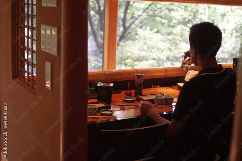 Man eating and drinking at a Japanese restaurant, looking out the ...