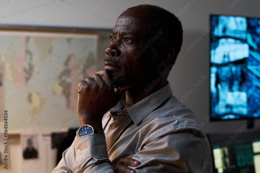 Man thoughtfully analyzing data in modern office environment featuring large map and multi ...