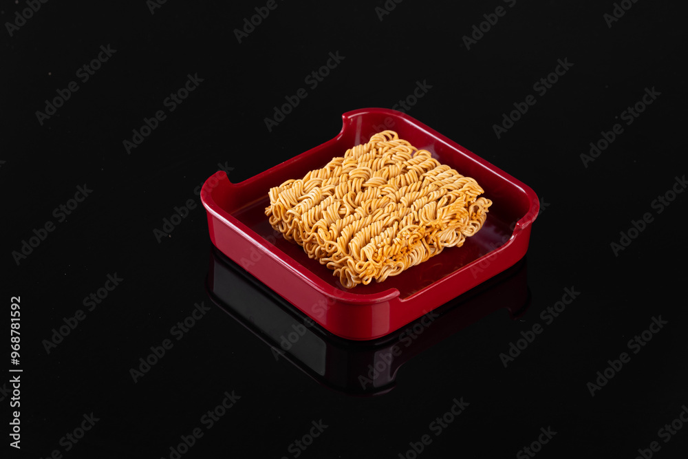 Square-shaped instant ramen noodle block in a red container on a black ...