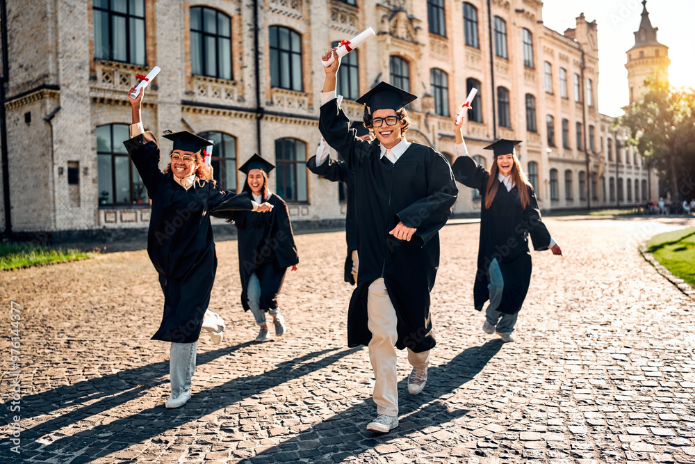 Happy smiling students running with diplomas at sunset near the ...