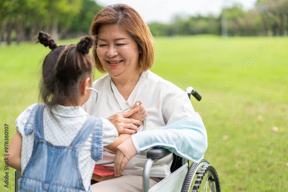 Little girl playing doctor with grandmother in a wheelchair at the park ...