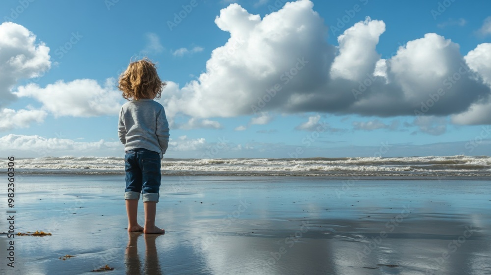 A young child standing on a beach, looking out at the rising sea levels ...