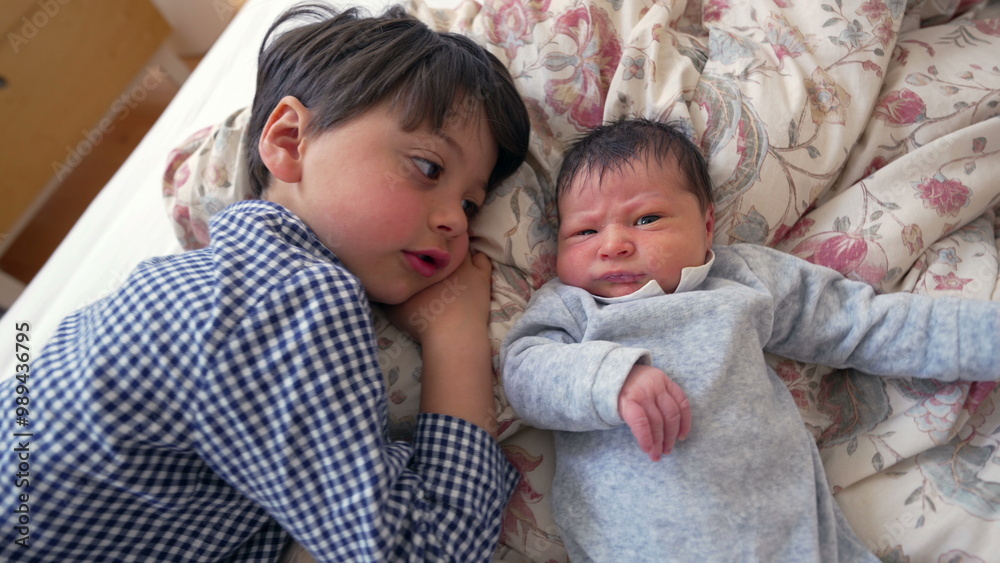 Older brother lying side by side with newborn sibling on a bed, sharing ...