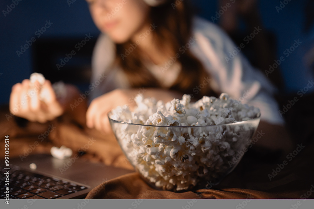 Teenage girl eats popcorn lying on bed at night watching interesting ...