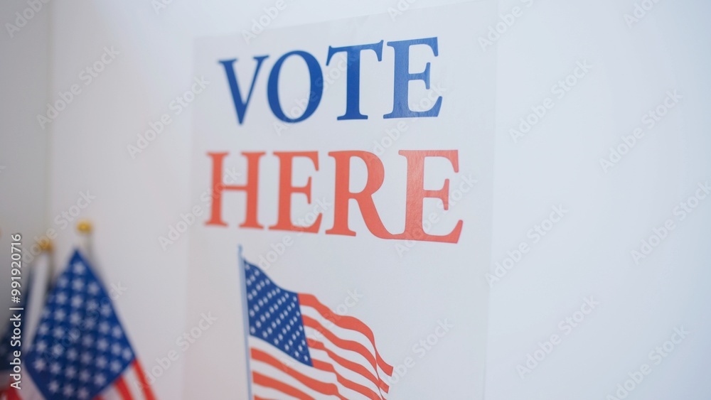 Camera focus on writing on white wall. Sign saying "vote here ...