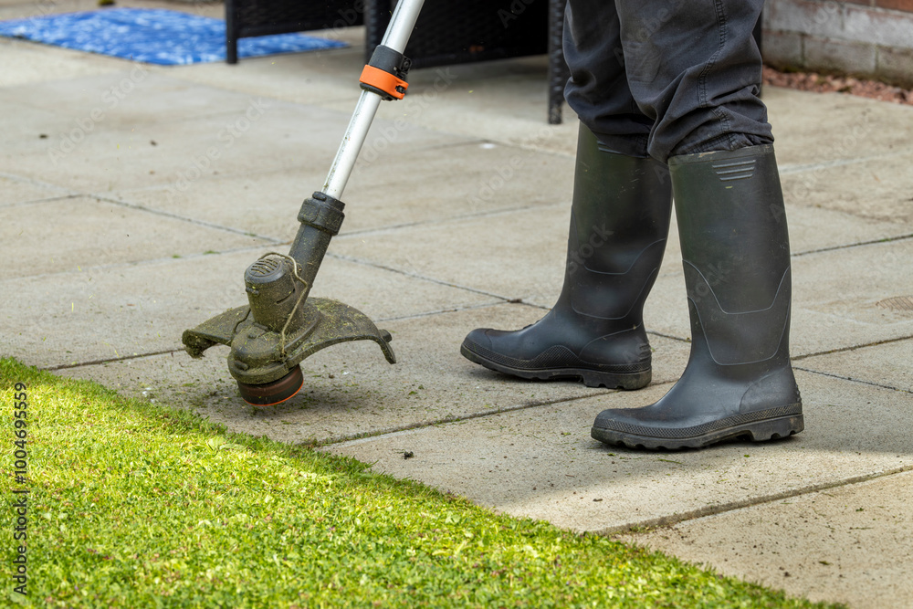 Woman in black trouser pants and wellie boots using electric strimmer ...