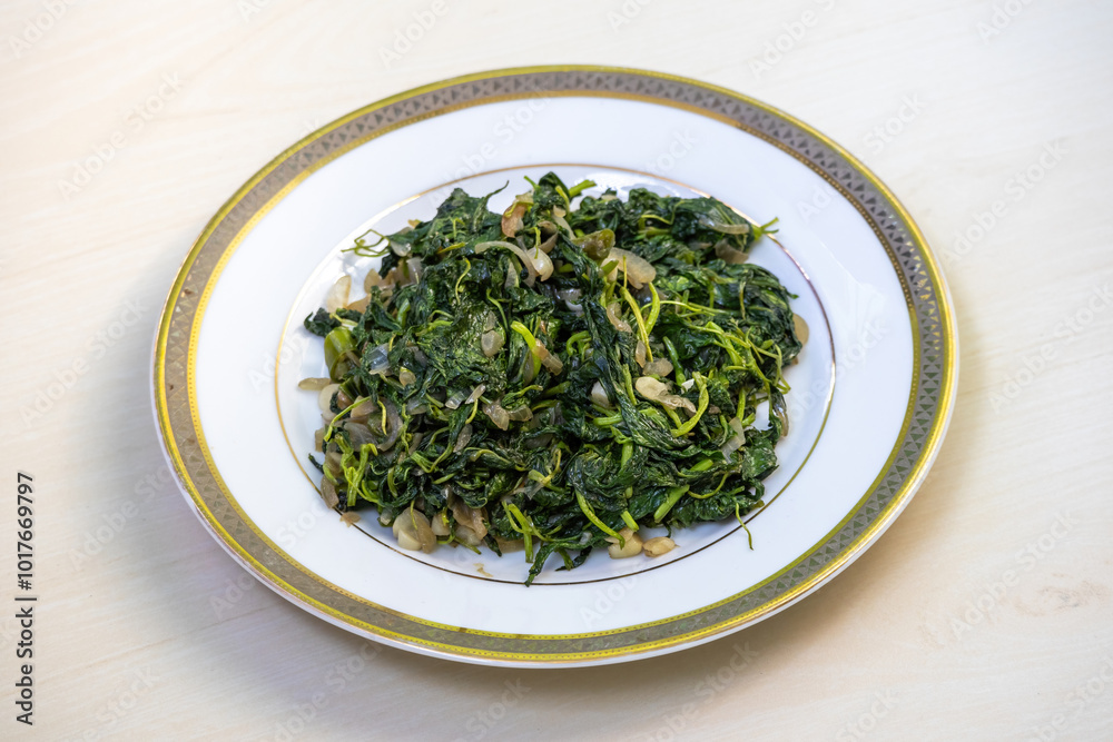 Stir-fried jute leaves, served in a white plate on a light wooden ...