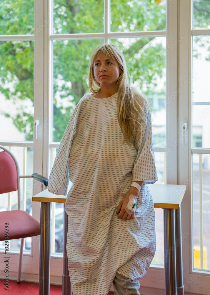 Young woman walking slowly through hospital after surgery with an ...