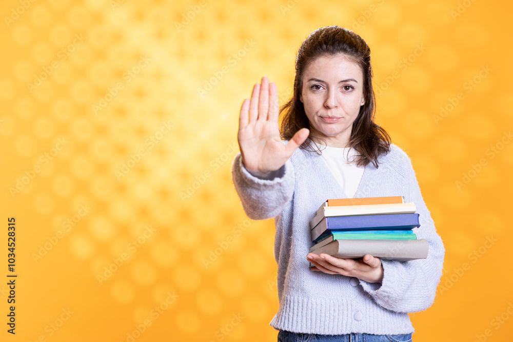Portrait of woman holding stack of books doing stop sign gesturing ...