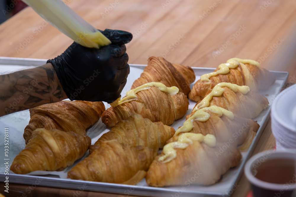 Close-up side view of cook decorating fresh baked croissant with ...